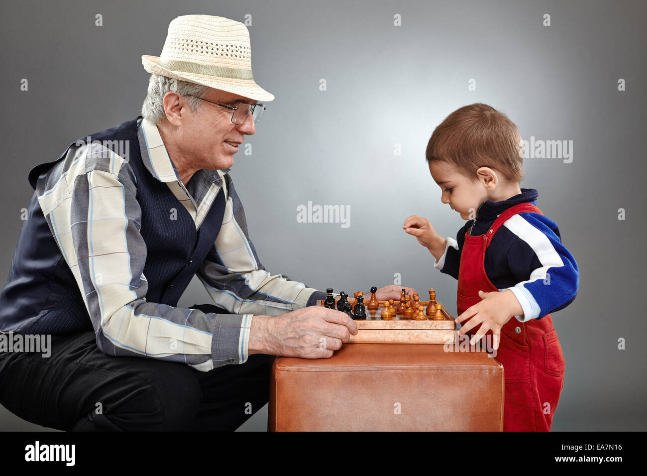 Grandpa and grandson playing a game of chess over gray background Stock ...