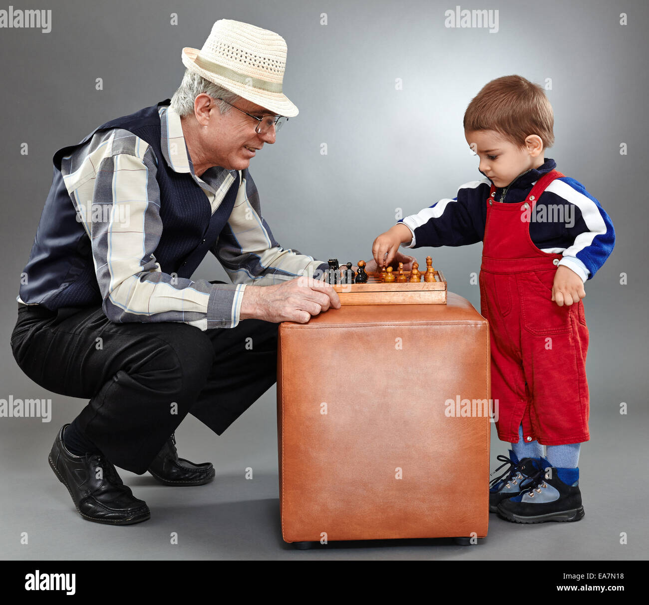 Grandpa and grandson playing a game of chess over gray background Stock ...