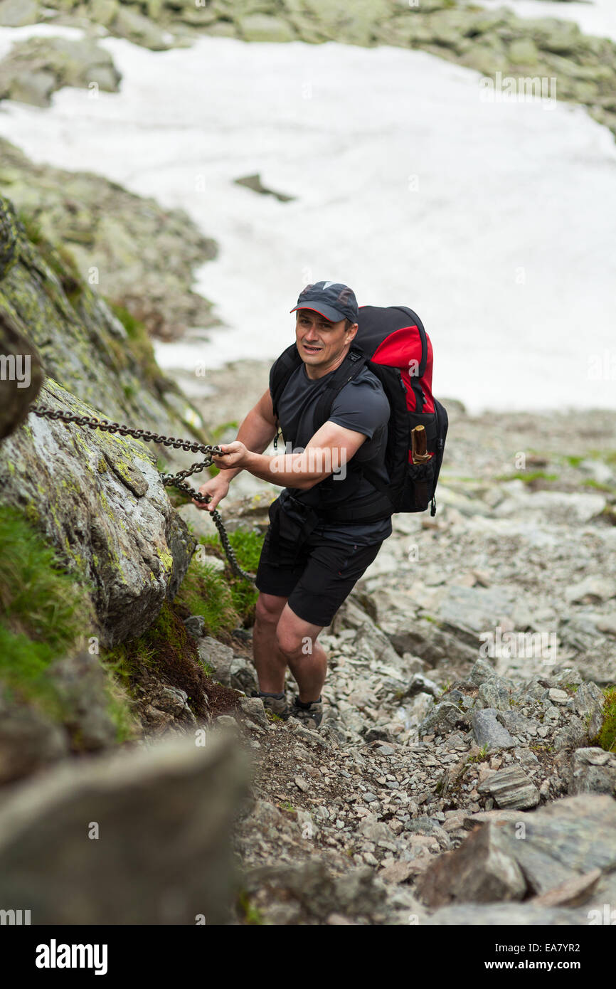 Man with heavy backpack climbing on safety cable on a mountain Stock ...
