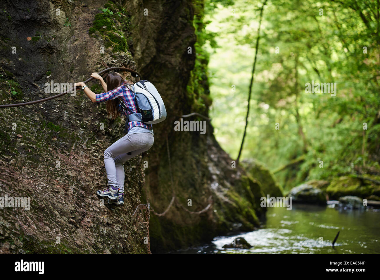 Young woman hiker climbing on safety cables in a gorge above the river ...