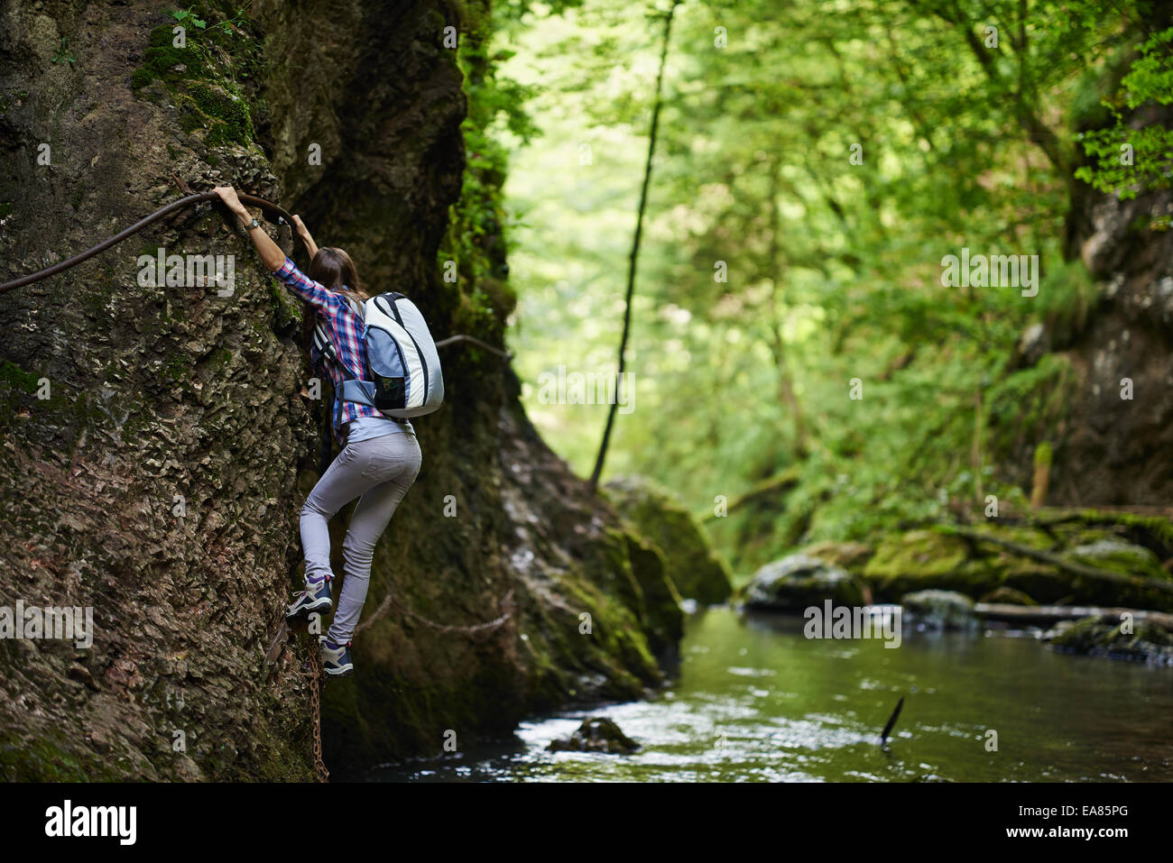 Young woman hiker climbing on safety cables in a gorge above the river ...