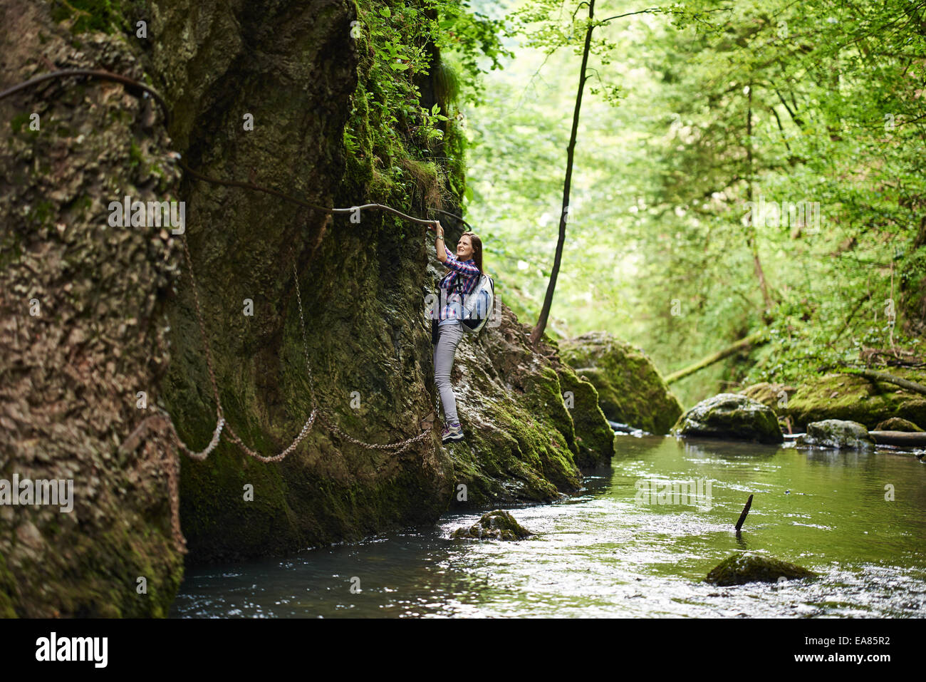 Young woman hiker climbing on safety cables in a gorge above the river ...