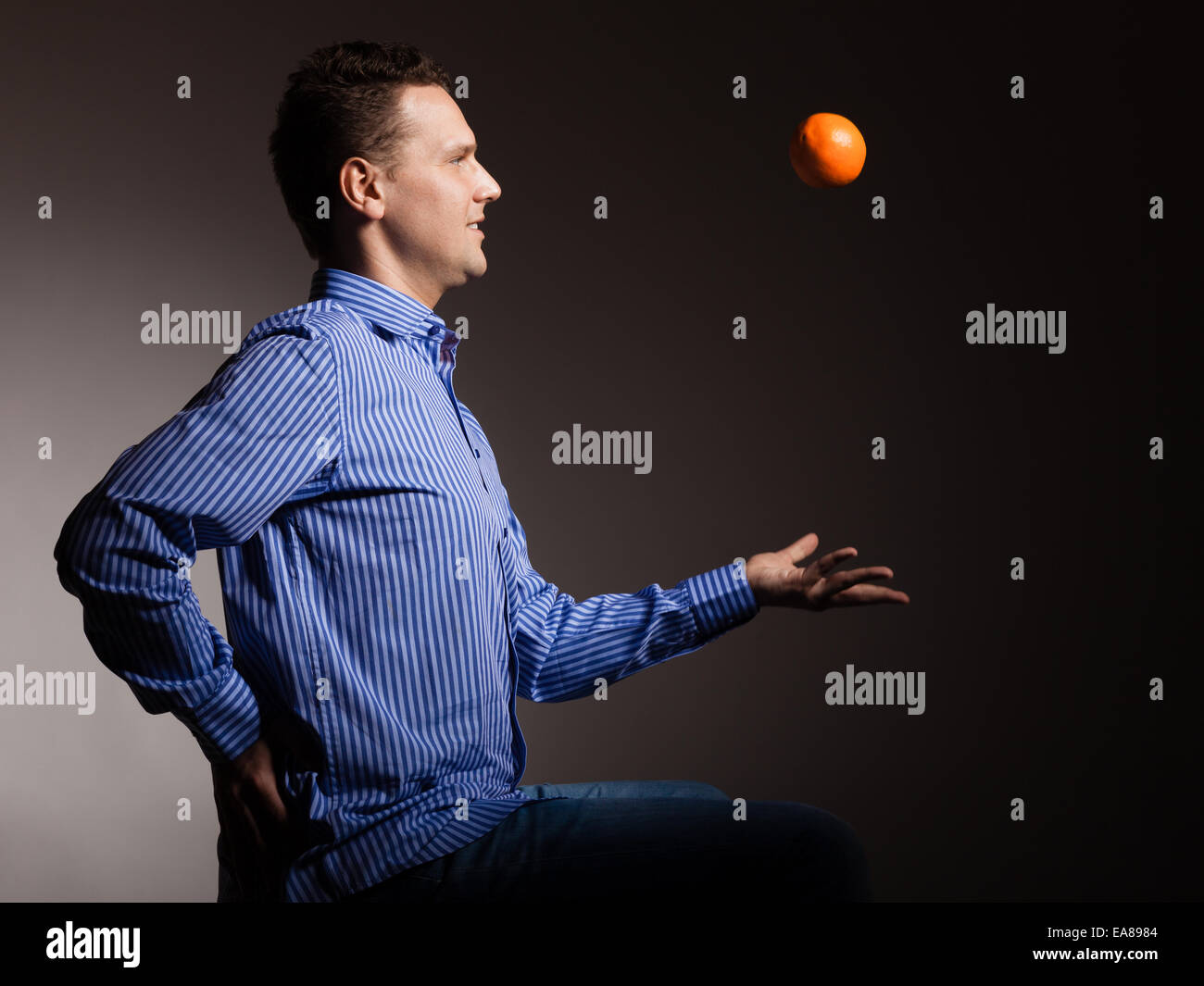 Diet and nutrition. Young smiling man throwing orange tropical fruit on ...