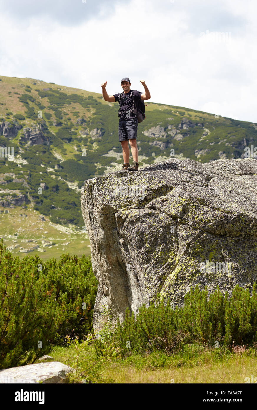 Happy caucasian hiker climbed on a massive rock making thumbs up sign ...