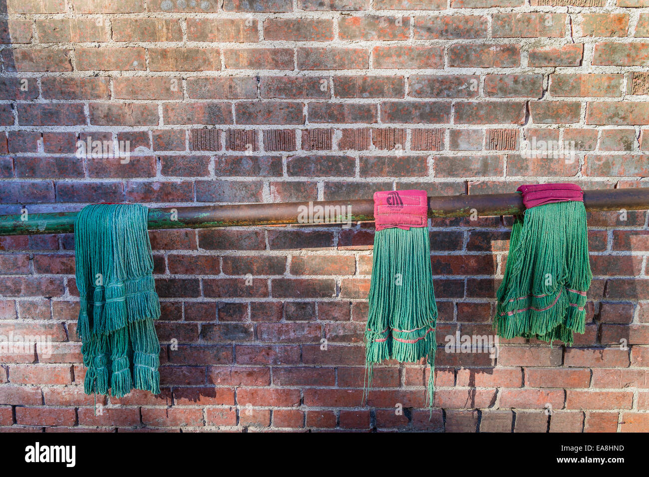 Three mop heads hanging to dry from a railing against a brick wall ...
