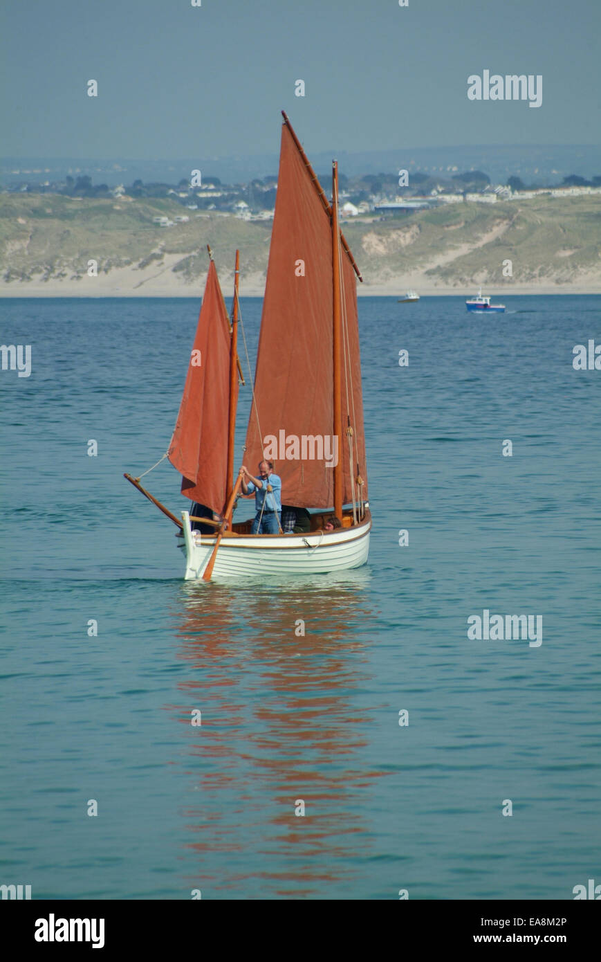 White hulled brown sailed Lugger sailing in St Ives Bay with man using ...