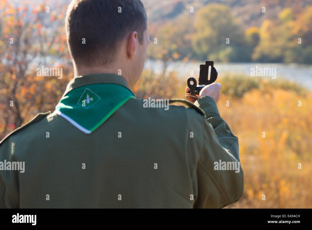 Scout taking a sighting with his compass facing out over a rural river ...