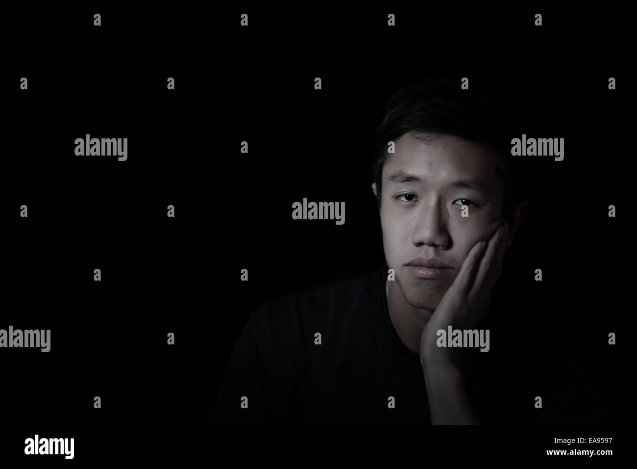 Young man, looking forward, showing depression with black background ...