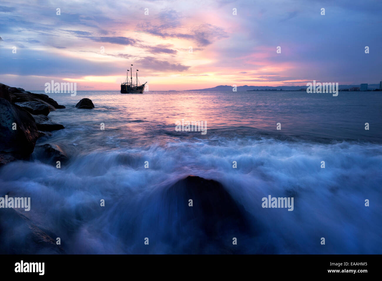 A Pirate Ship sails along the ocean at sunset as the waves roll into ...