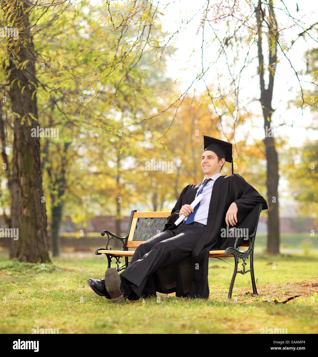 Graduate student holding diploma seated on bench in park shot with tilt ...