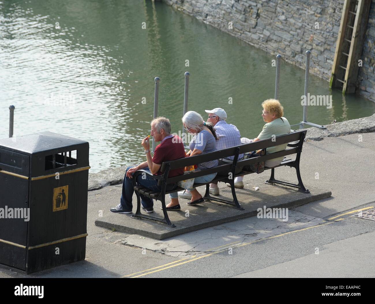 four people sitting on a bench in Padstow harbour, Cornwall,England uk ...
