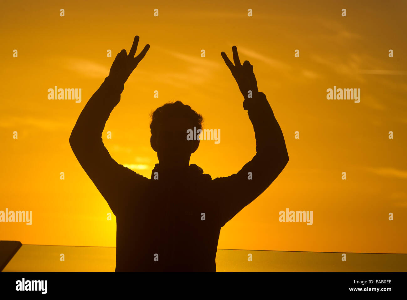 Silhouette of a man at sunrise giving the peace / victory hand sign ...