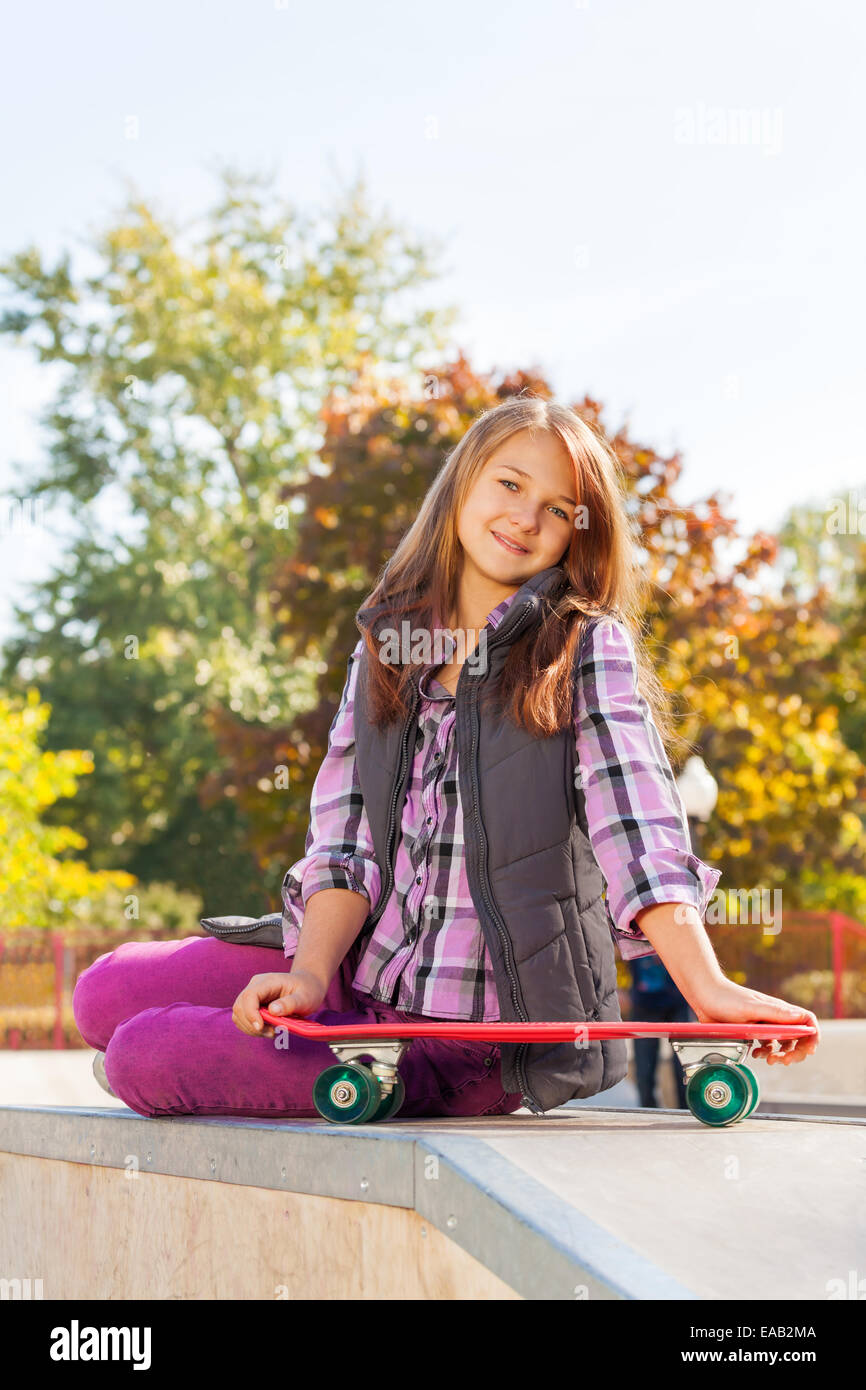 Positive girl holds skateboard sits on ground Stock Photo - Alamy
