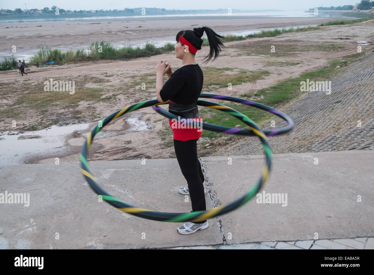 Woman using hoola hoops exercise on bank of Mekong River in Vientiane ...