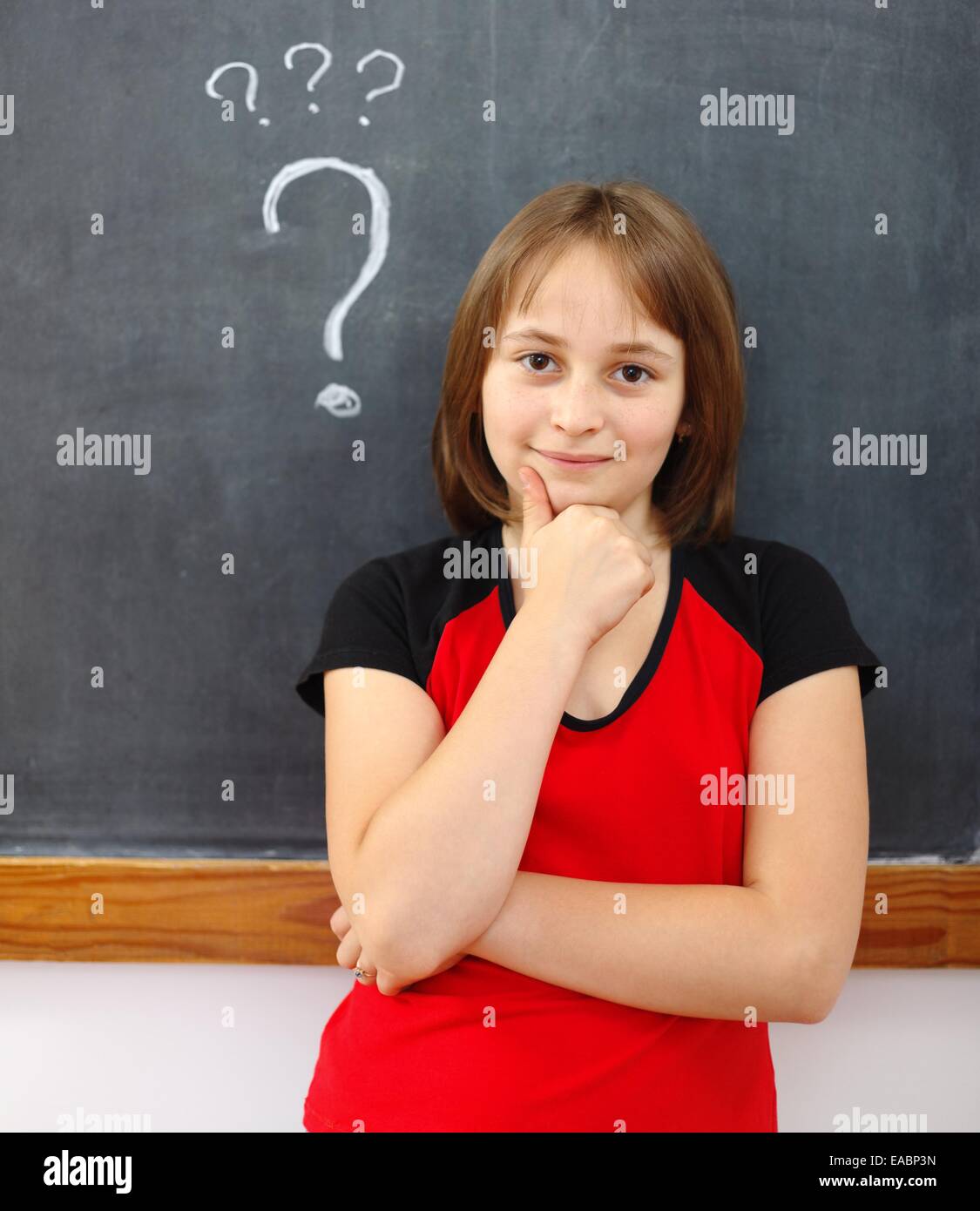 Elementary school girl thinking at chalkboard, question mark behind her ...