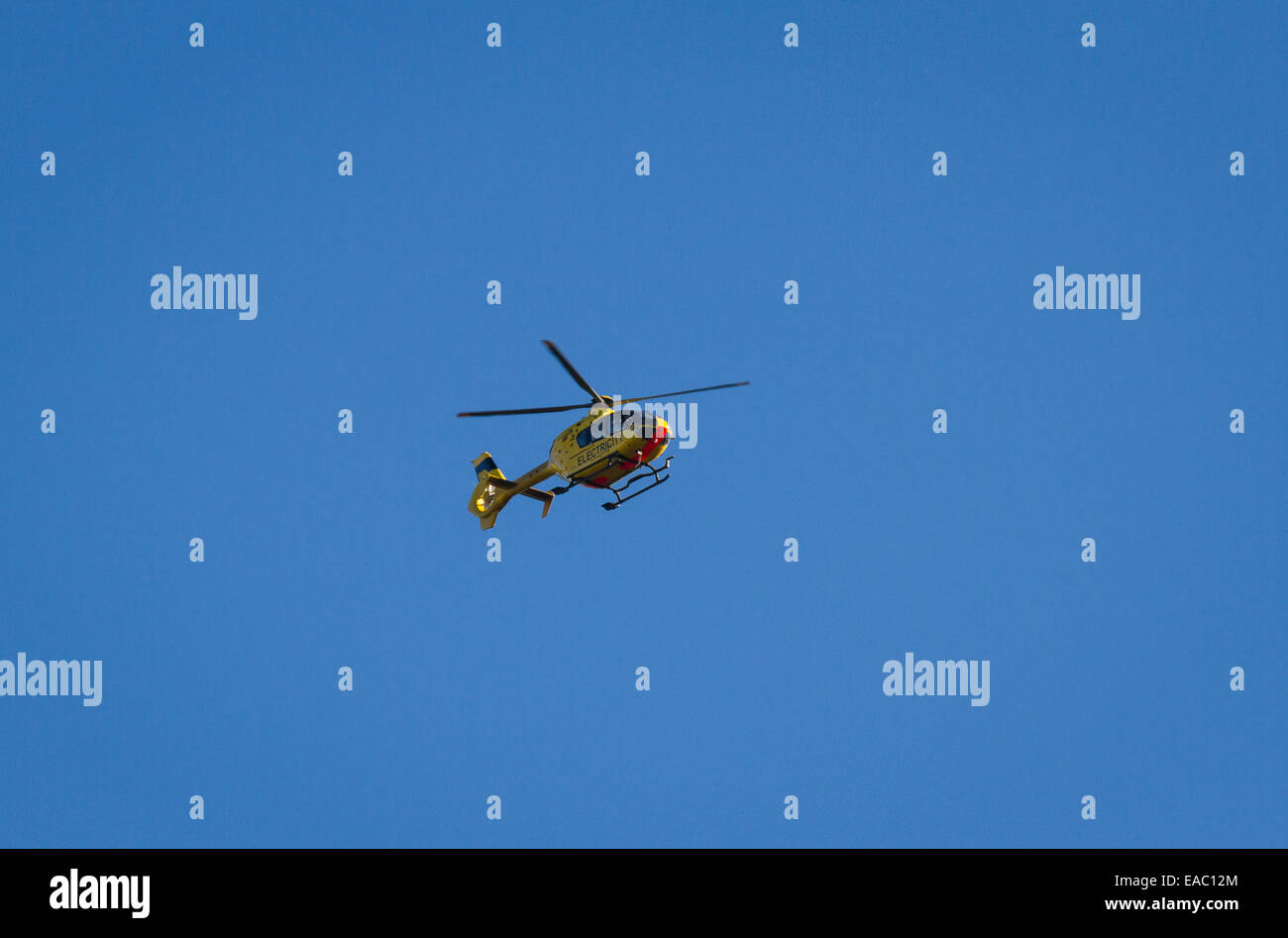 A yellow helicopter used for surveying power lines flying in a clear ...