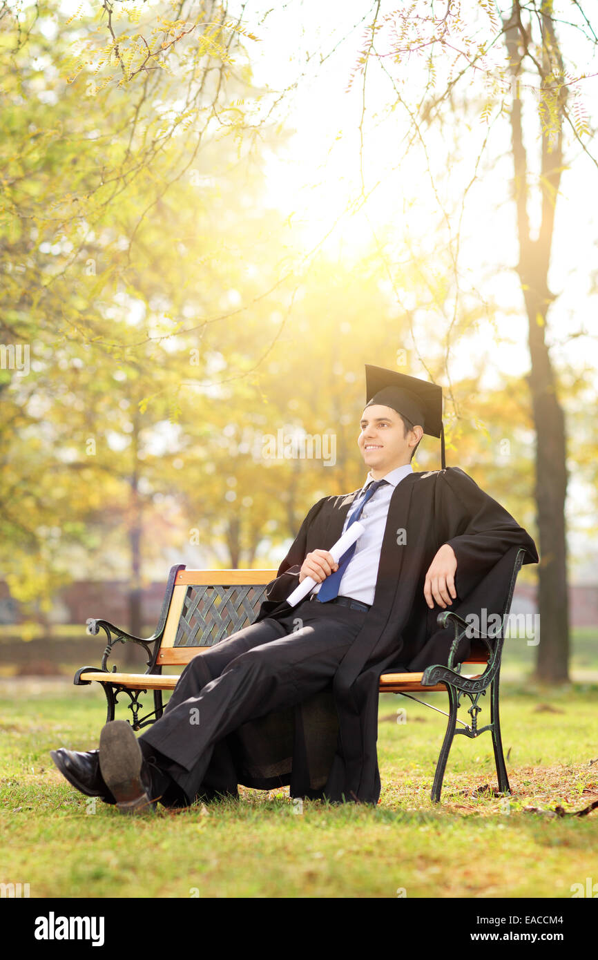 Relaxed graduate sitting on a bench in park in autumn Stock Photo - Alamy