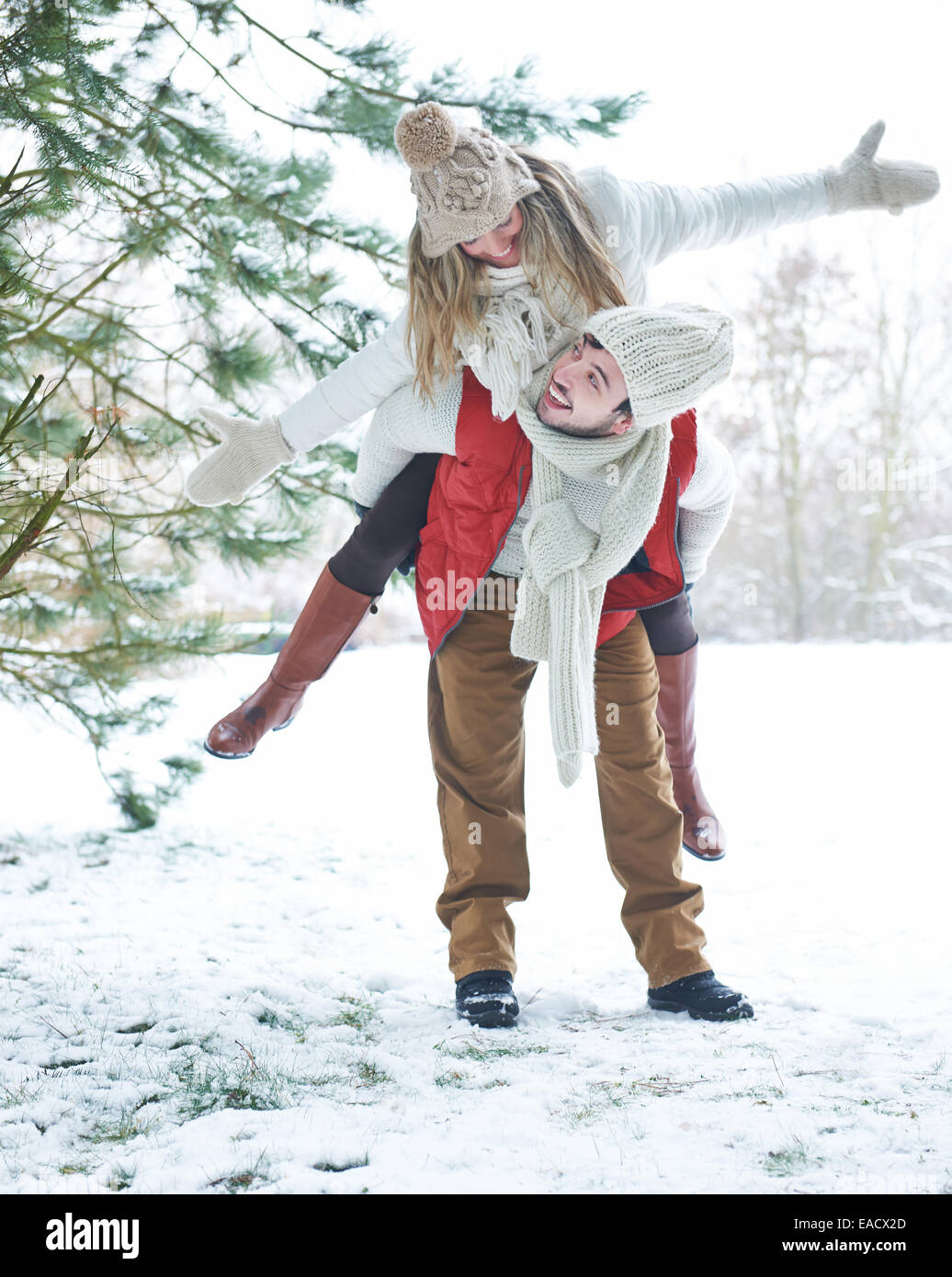 Happy man giving smiling woman a piggyback ride through snow in winter ...