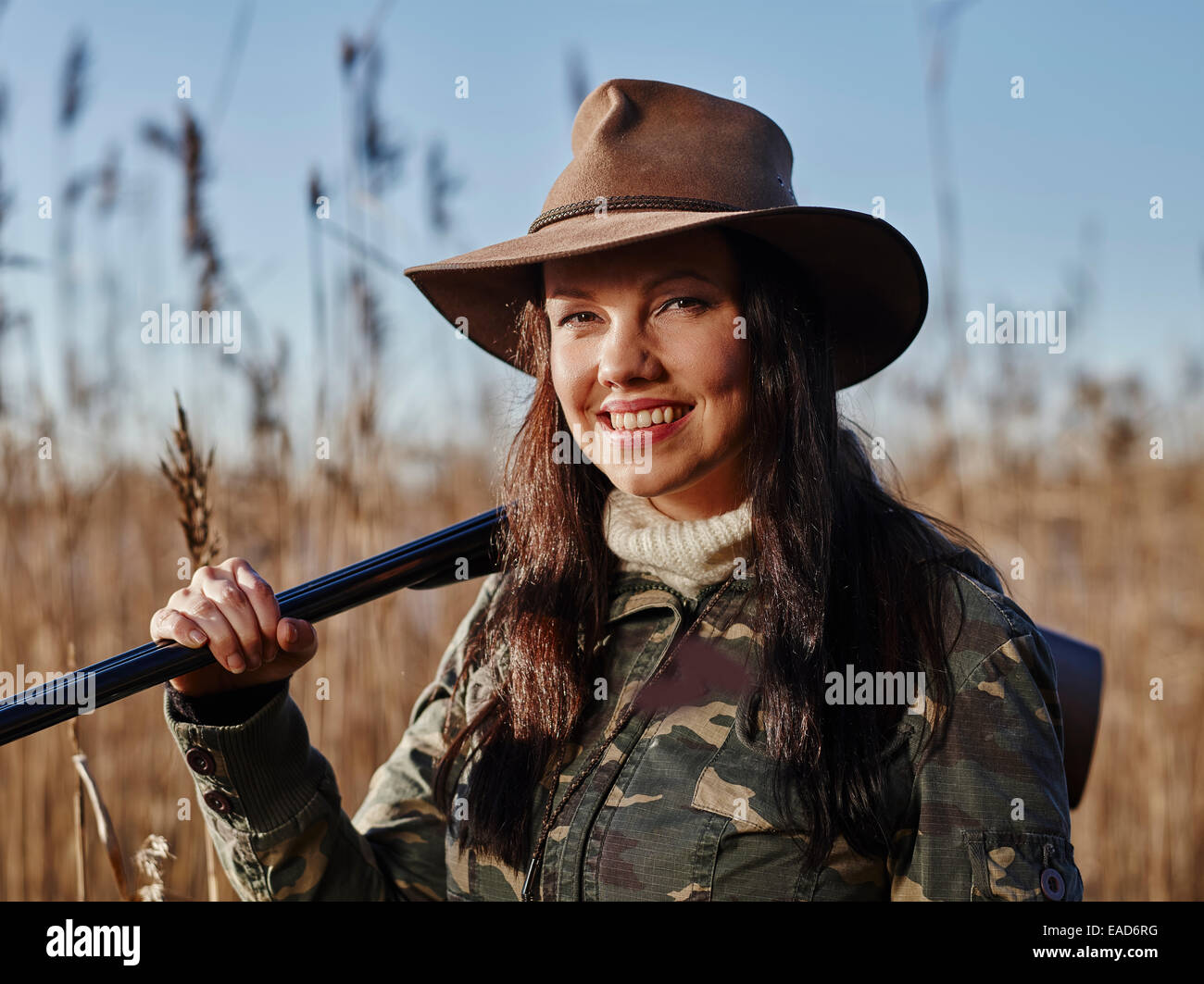 Waterfowl hunting, smiling female hunter carry a shotgun and she looks ...