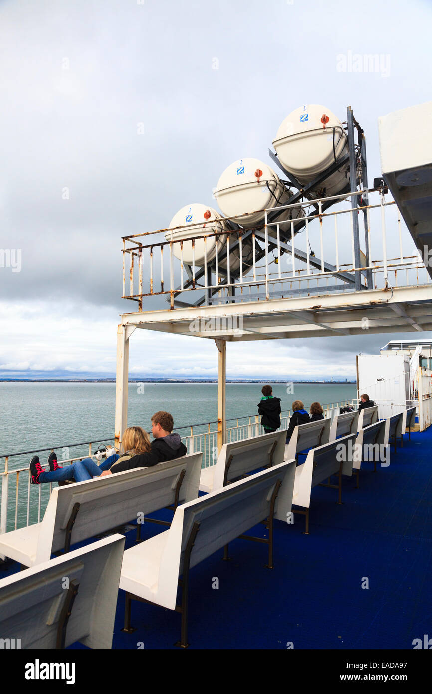 Passengers sitting on seats on a deck of a ferry under a Zodiac ...