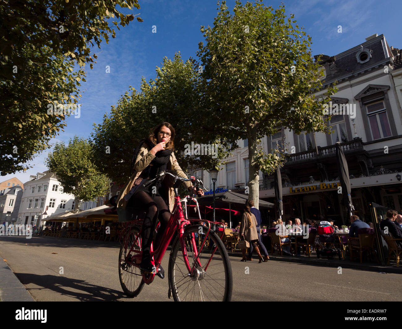 Young woman riding a bicycle in front of the cafes in Vrijthof square ...