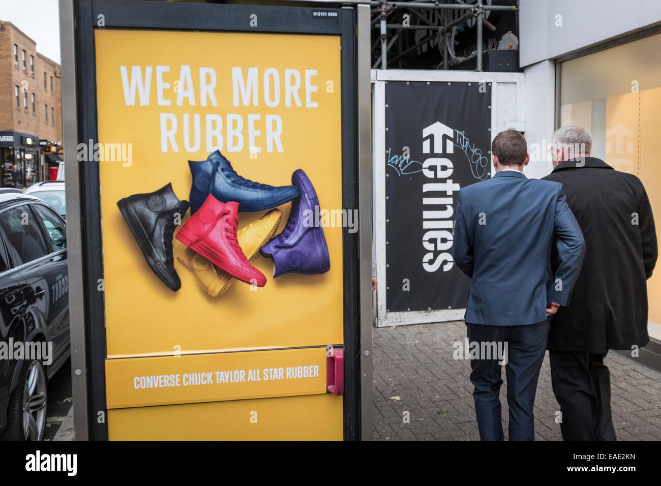 Two men walking past a colourful advert for rubber shoes Stock Photo ...