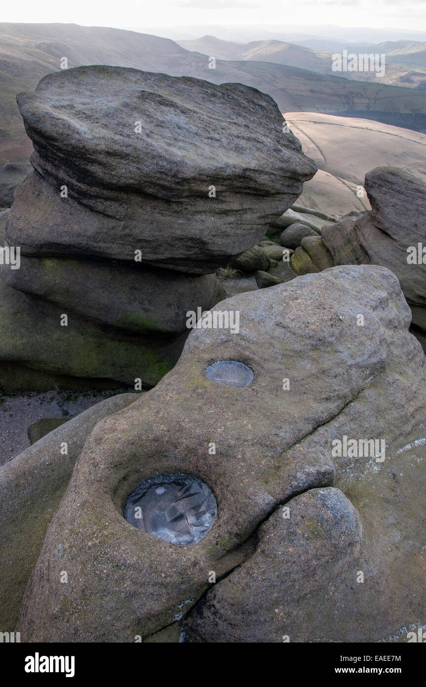 Gritstone rock formations including pools of frozen water on the edge ...
