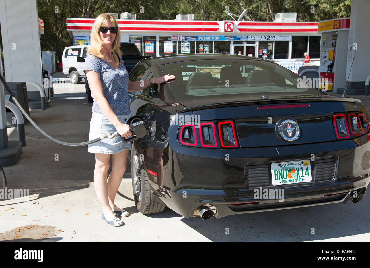 Woman motorist at a gas station filling a black Ford Mustang sports car ...