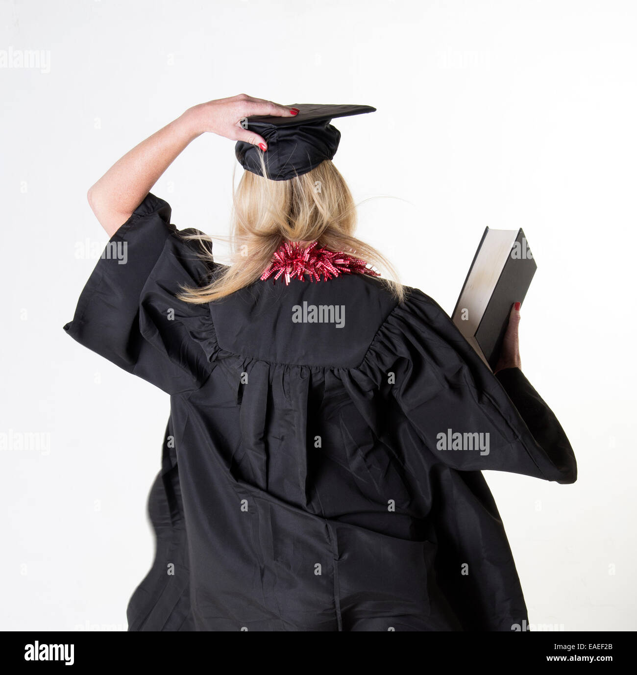 Mature female university graduate student wearing cap and gown holding ...