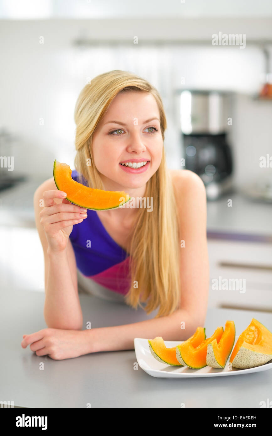 Happy young woman eating melon in kitchen Stock Photo - Alamy