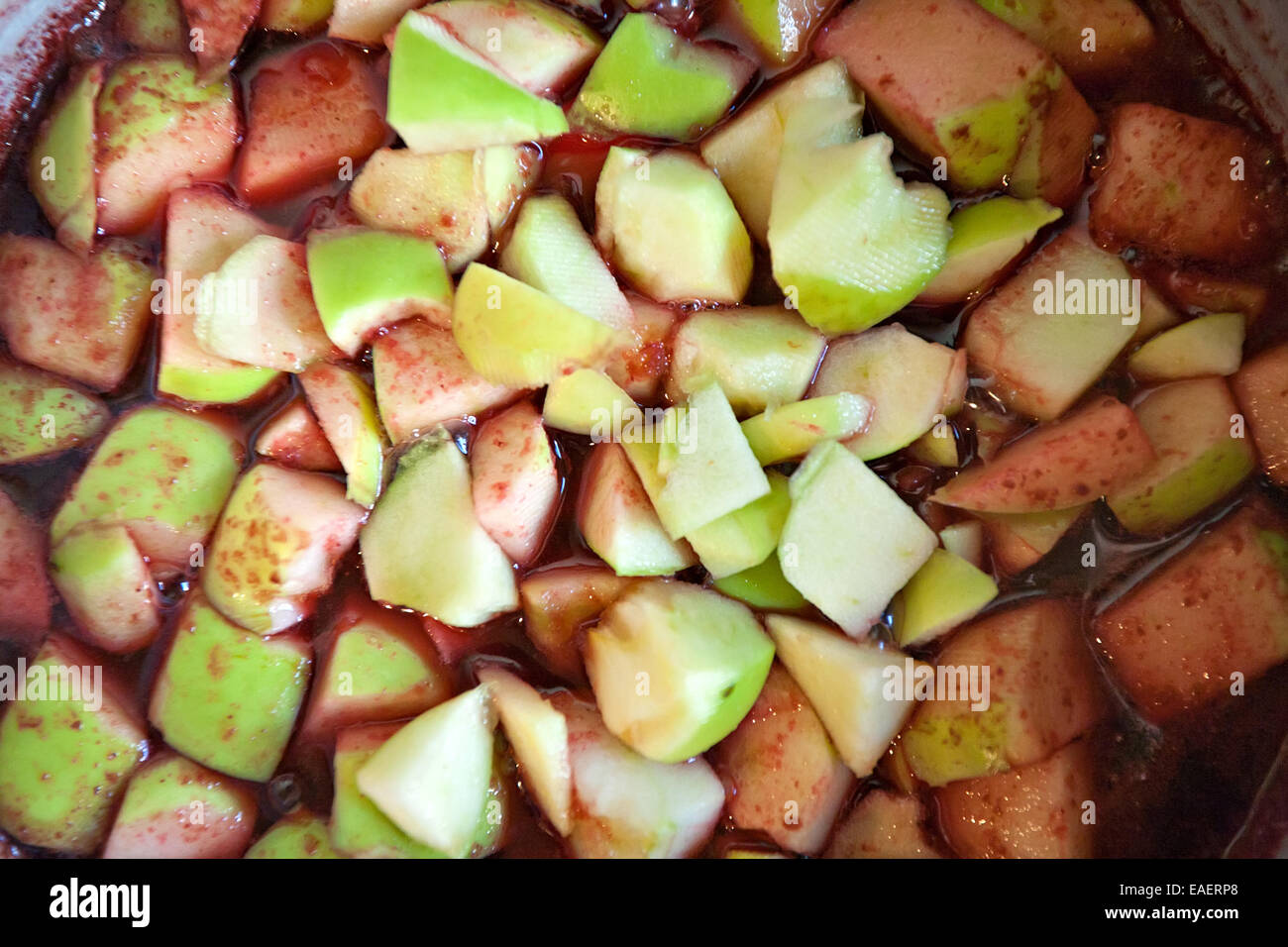 apple pieces boiled in red syrup for homemade compote surface closeup ...