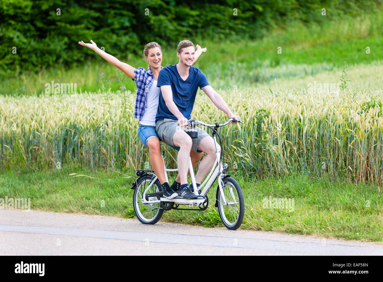 Man and woman, a couple, riding together tandem bike on country lane ...