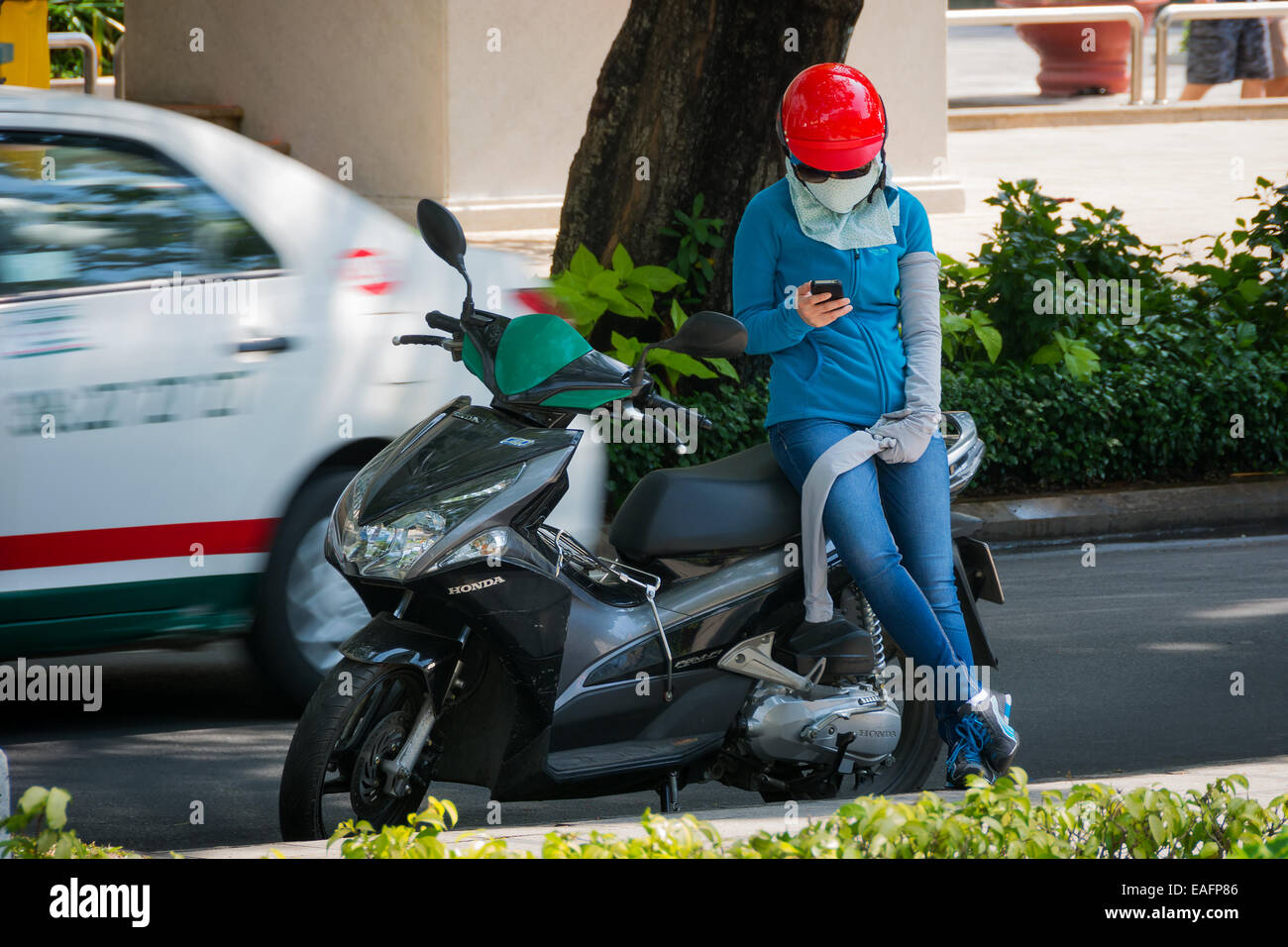 Vietnamese girl busy texting leaning against her motorcycle Stock Photo ...