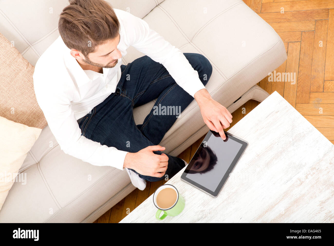 A young adult man sitting on the couch using a tablet Stock Photo - Alamy