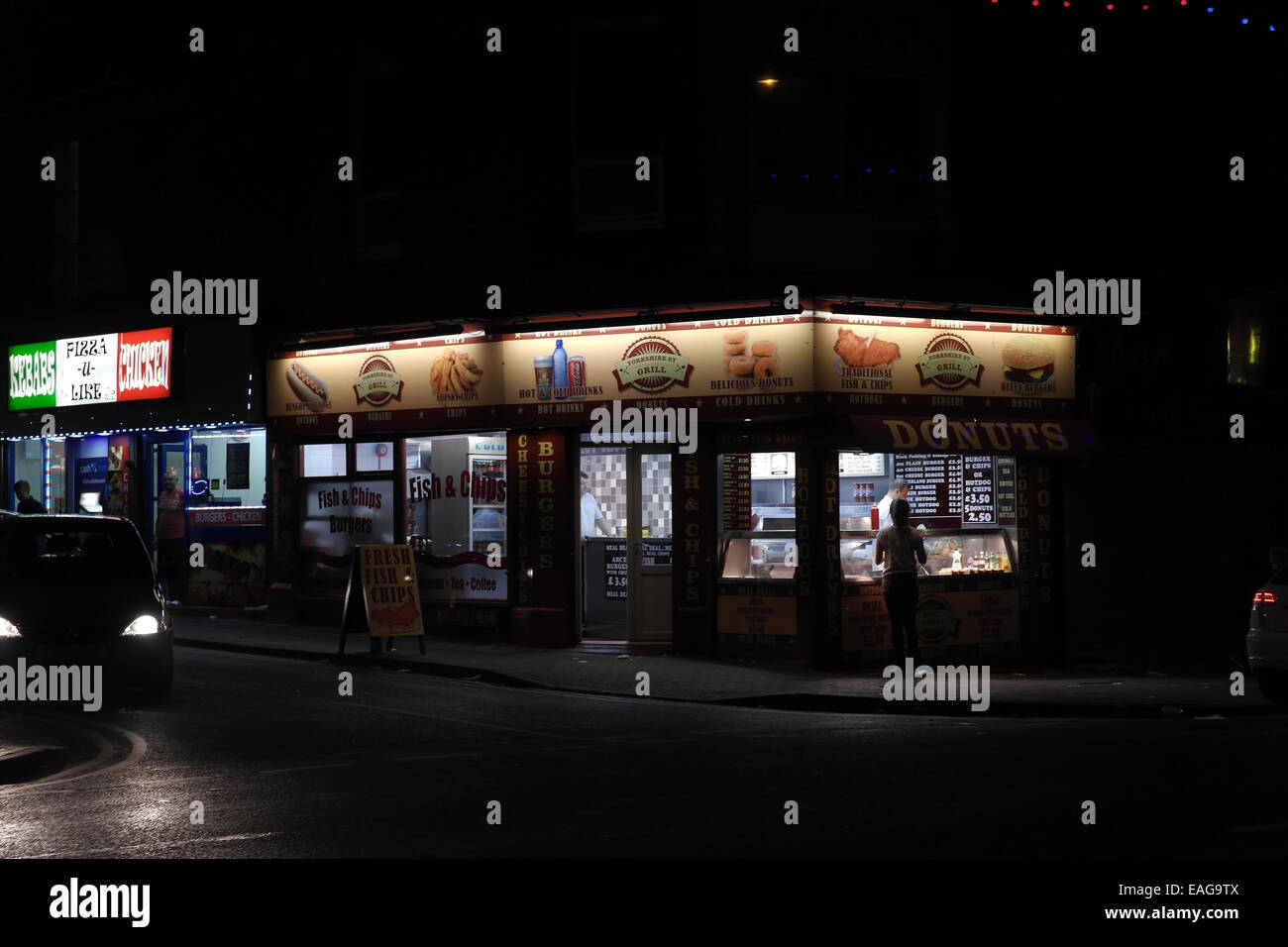 Night view woman buying food at illuminated street corner shop selling ...