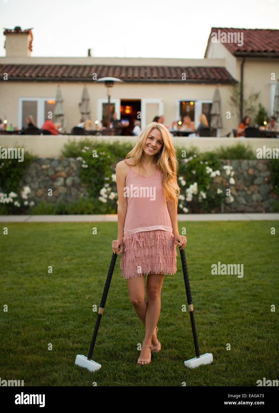 A pretty young girl stands against two croquet mallets on her two sides ...