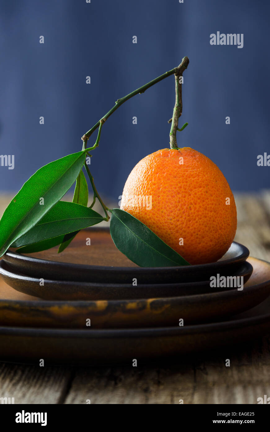 Single ripe tangerine on brown plates over wooden table Stock Photo - Alamy