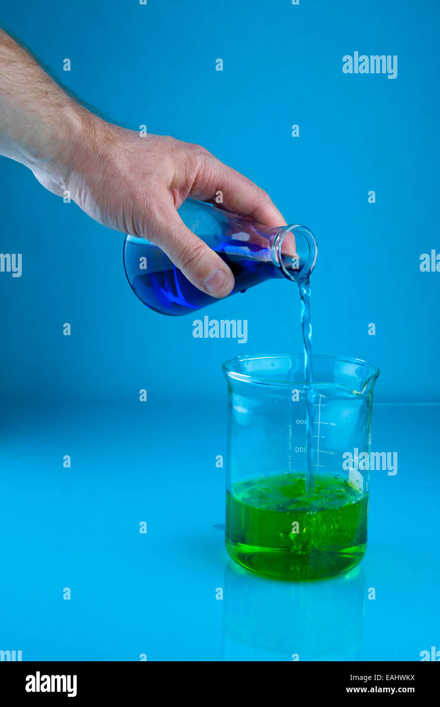 Pouring a blue liquid into a beaker of a yellow liquid, making a green ...