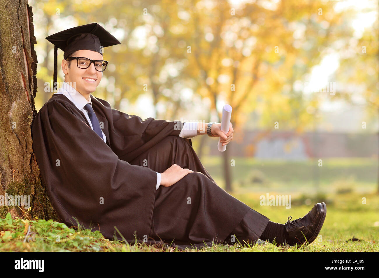 Graduate student sitting by a tree in a park Stock Photo - Alamy