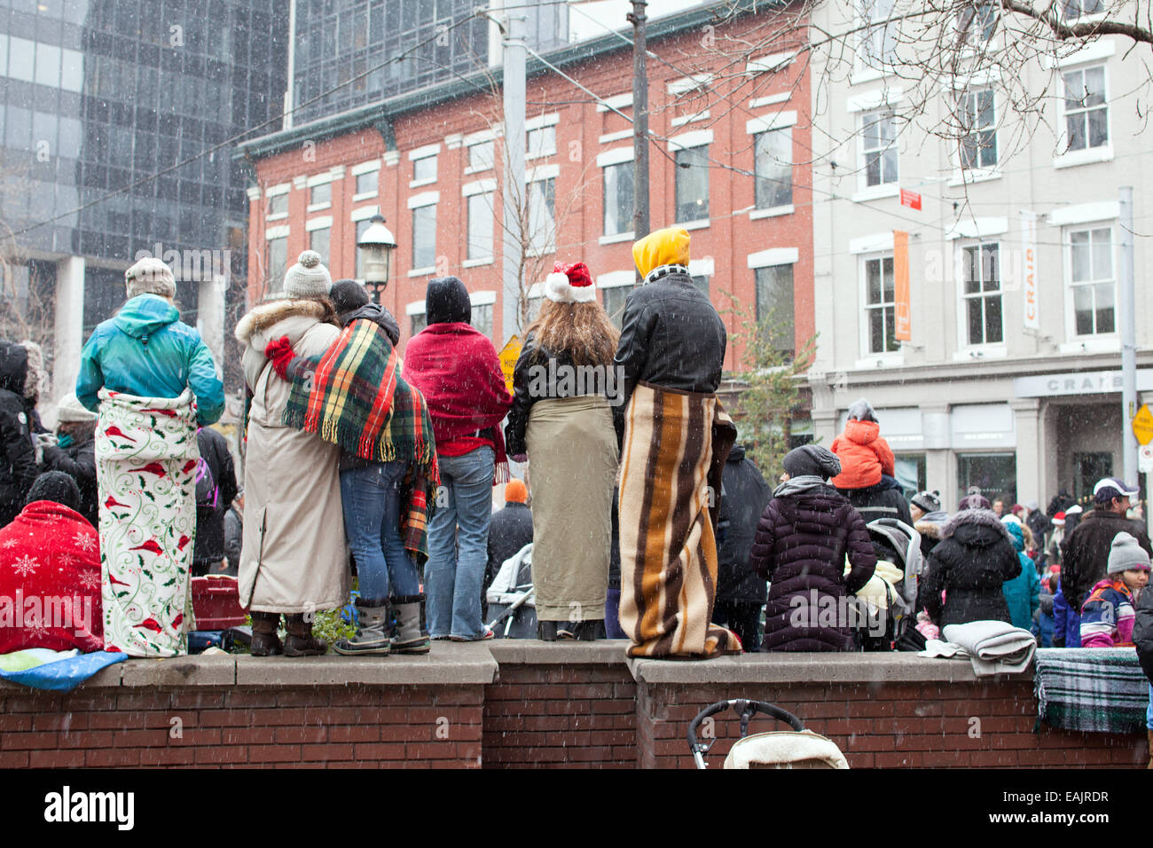 People wrapped in blankets watching Santa Claus Parade under falling ...