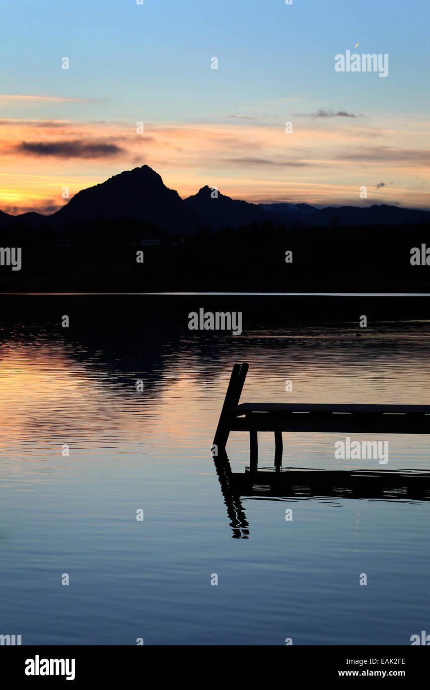 A pier is reflected in the surface of lake Hopfensee at the fringe of ...