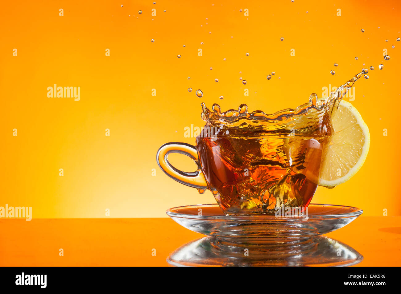 Cup of tea with splash on glass with orange background Stock Photo - Alamy
