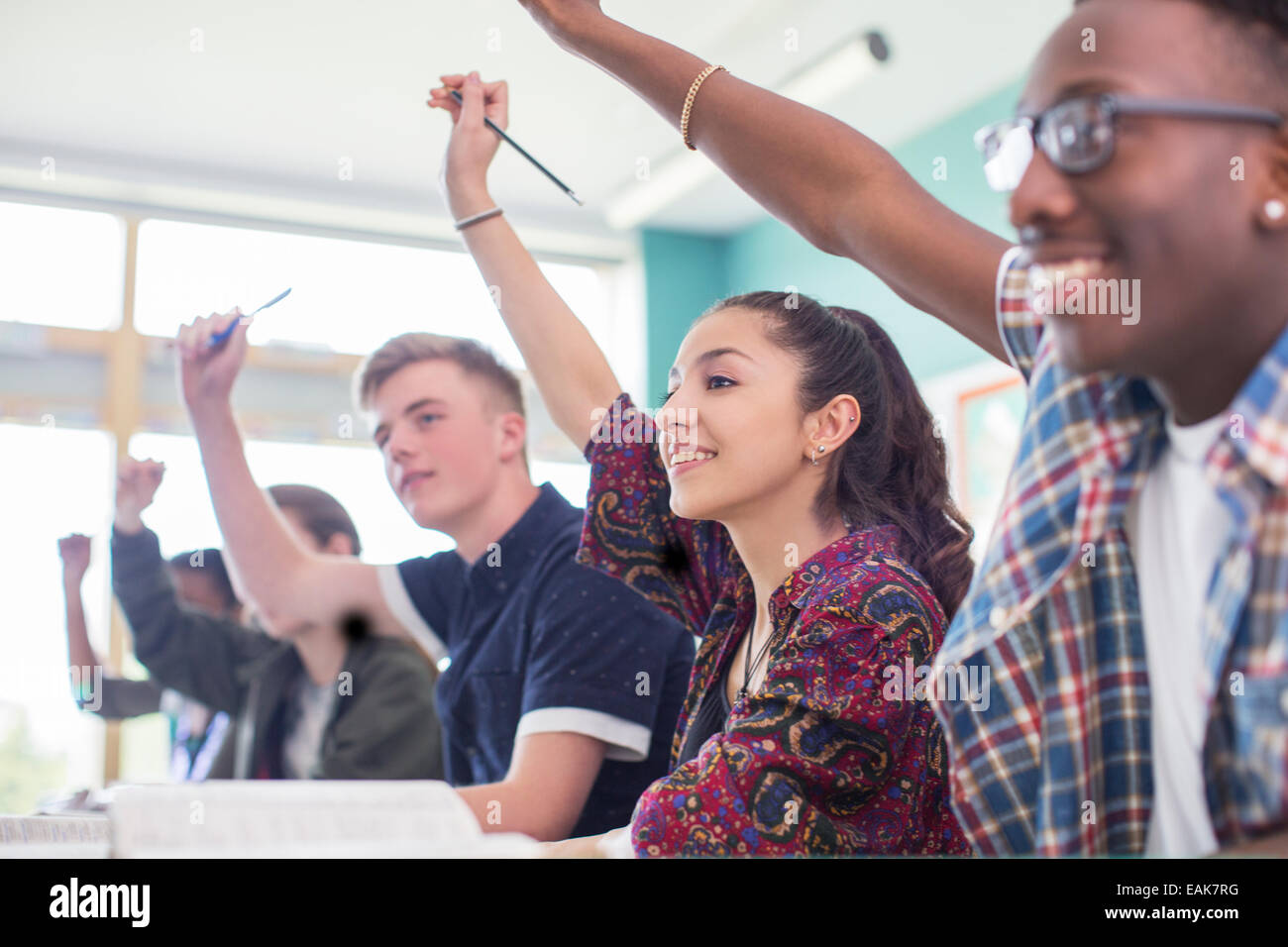 Students sitting in classroom during lesson, smiling and raising hands ...