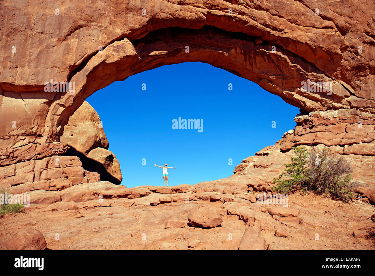 Girl standing in North Window Arch, a stone arch of red sandstone ...