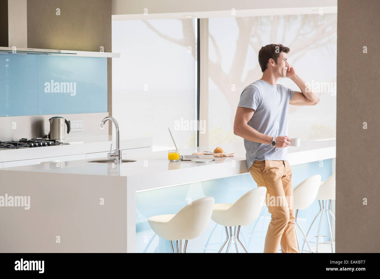 Man with coffee cup using phone in modern kitchen Stock Photo - Alamy
