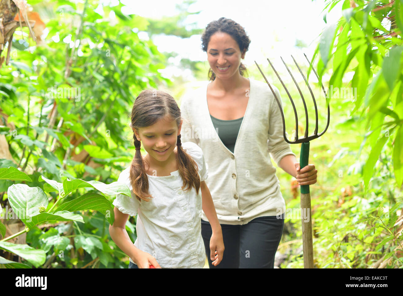 Girl and woman with gardening fork walking through plants in greenhouse ...