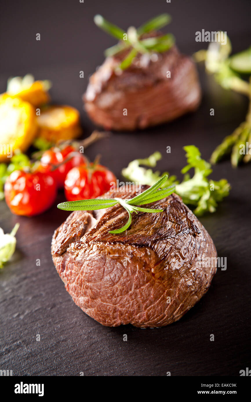 Pieces of red meat steaks with vegetable and spices, served on black ...