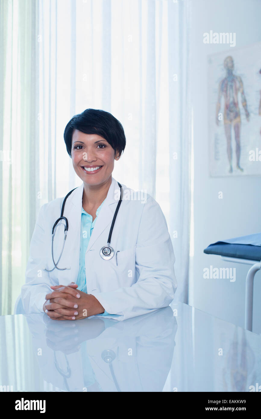 Portrait of smiling female doctor sitting at desk in office Stock Photo ...