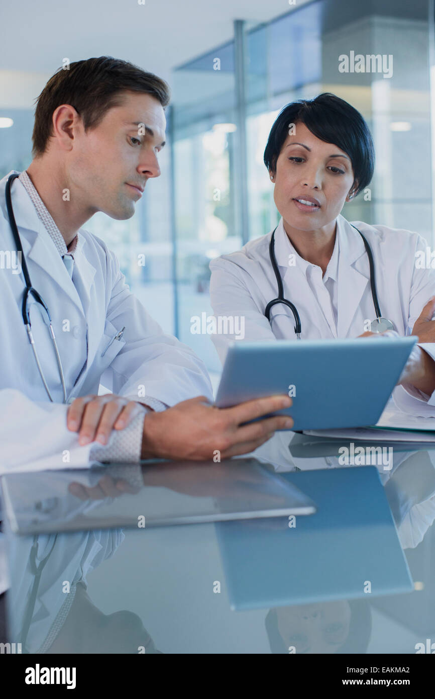 Doctors discussing patient's treatment at desk, using digital tablet ...