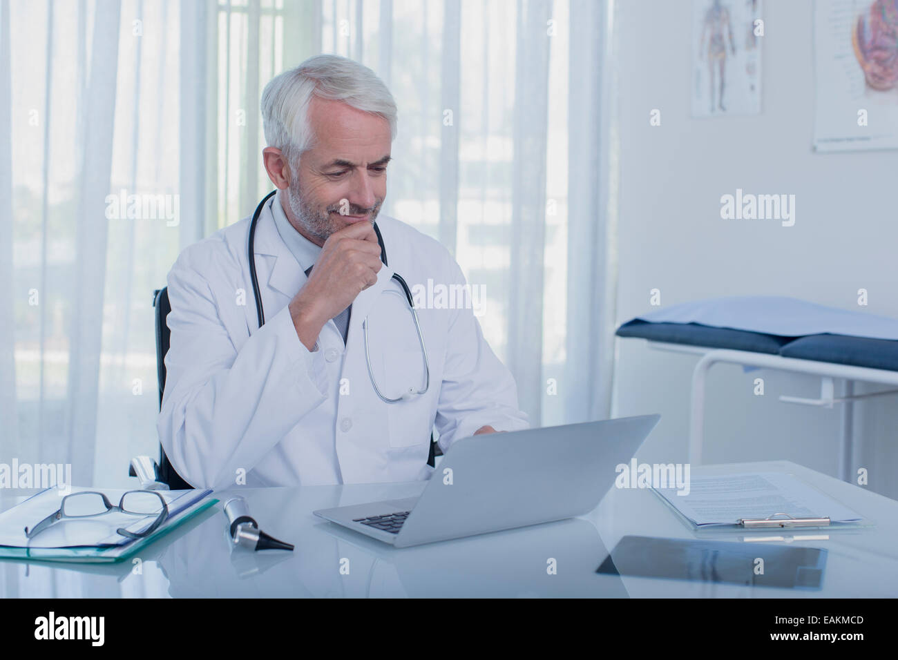 Smiling mature doctor sitting at desk with laptop in office Stock Photo ...